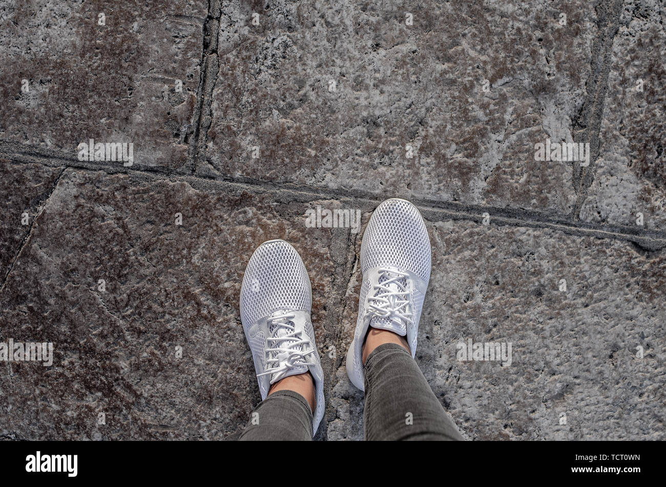Women's legs in white sneakers on the stone pavement Stock Photo - Alamy
