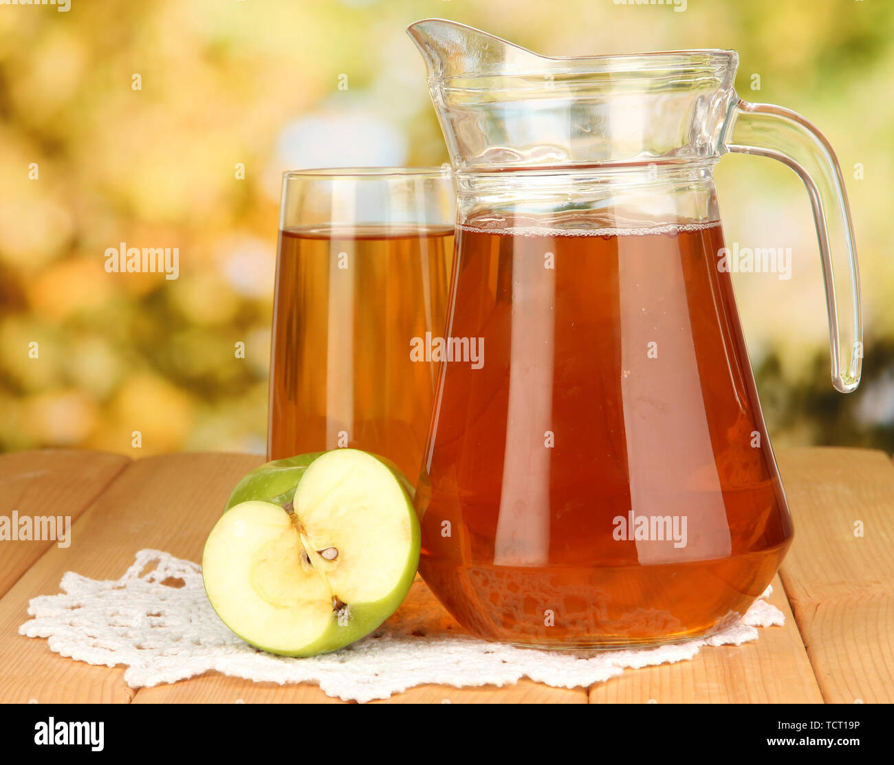Full glass and jug of apple juice and apples on wooden table outdoor ...