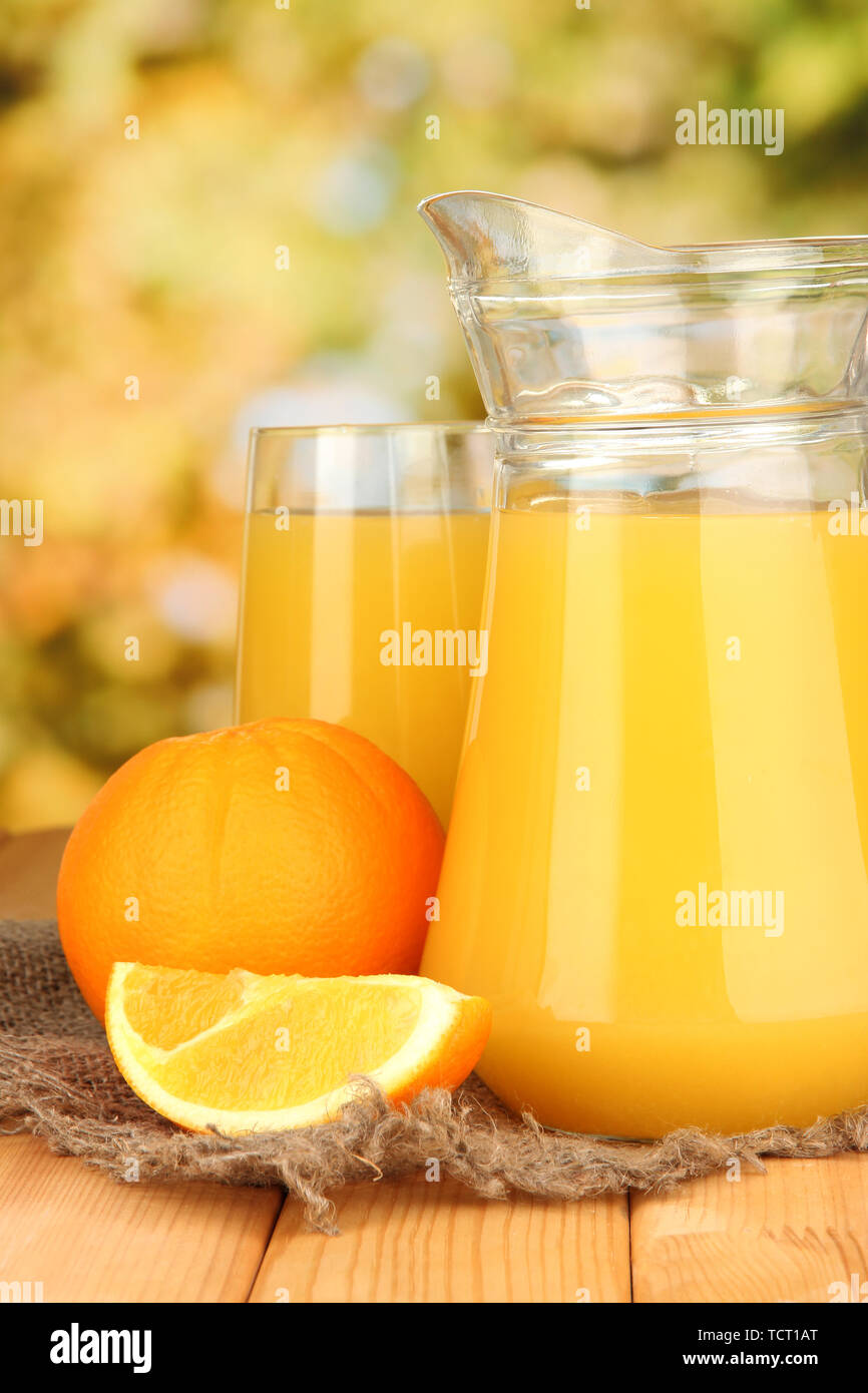 Full glass and jug of orange juice and oranges on wooden table outdoor ...