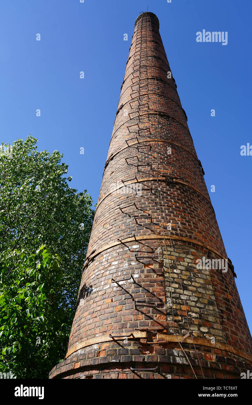 An old high factory chimney against a blue sky, built of red bricks ...