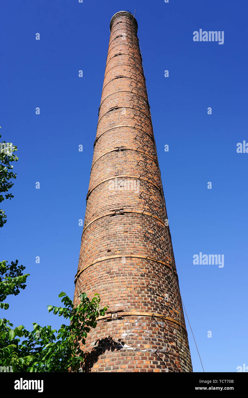 An old high factory chimney against a blue sky, built of red bricks ...