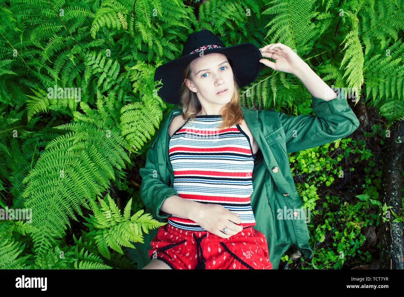 Pretty young blond girl hipster in hat among fern, vacation in green ...