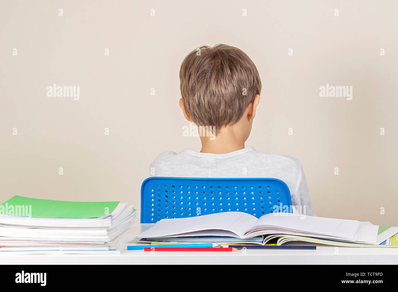 Sad kid sitting turn back at the table with pile of school books and ...