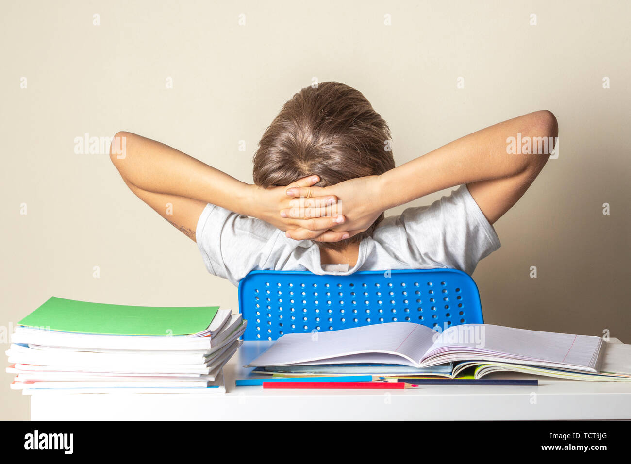 Sad kid sitting turn back at the table with pile of school books and ...