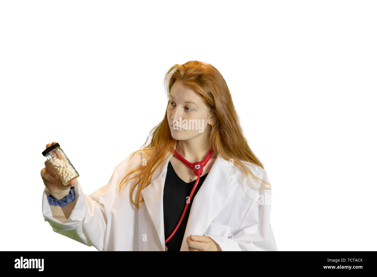 Red haired teen girl in lab coat and stethoscope holding bottle of ...