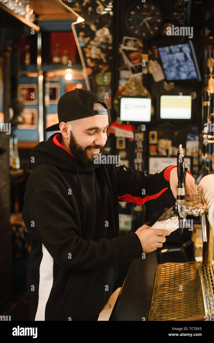 smiling barman pouring beer in a bar. Bearded courageous man pours you ...