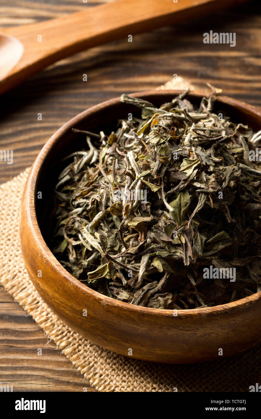 Heap of dried, raw white tea leaves in wooden bowl on bamboo mat ...