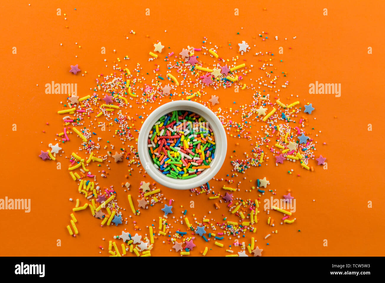 Sprinkles on bright orange background with little white bowl in middle ...
