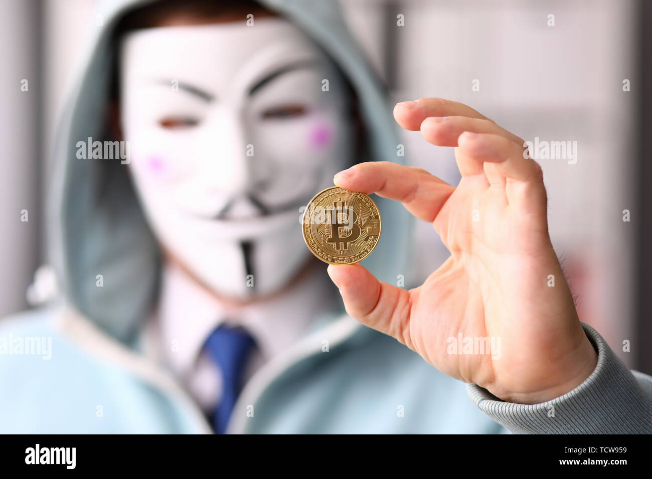 Hacker wear anonymus mask hold bitcoin in hand Stock Photo - Alamy