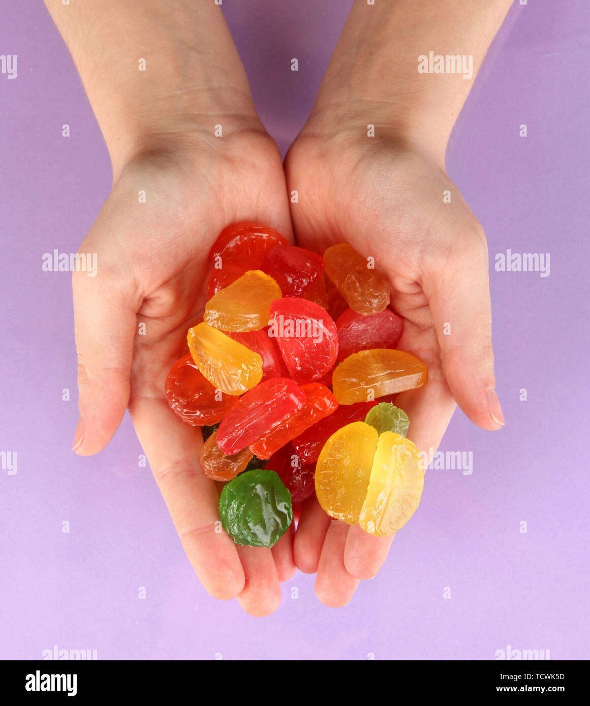 Hands full of sweets on purple background Stock Photo - Alamy
