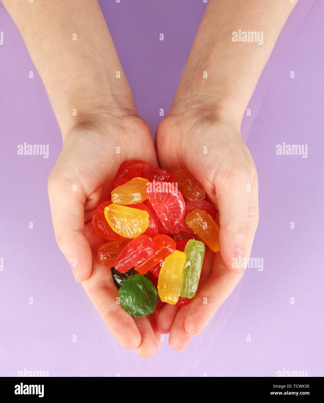 Hands full of sweets on purple background Stock Photo - Alamy