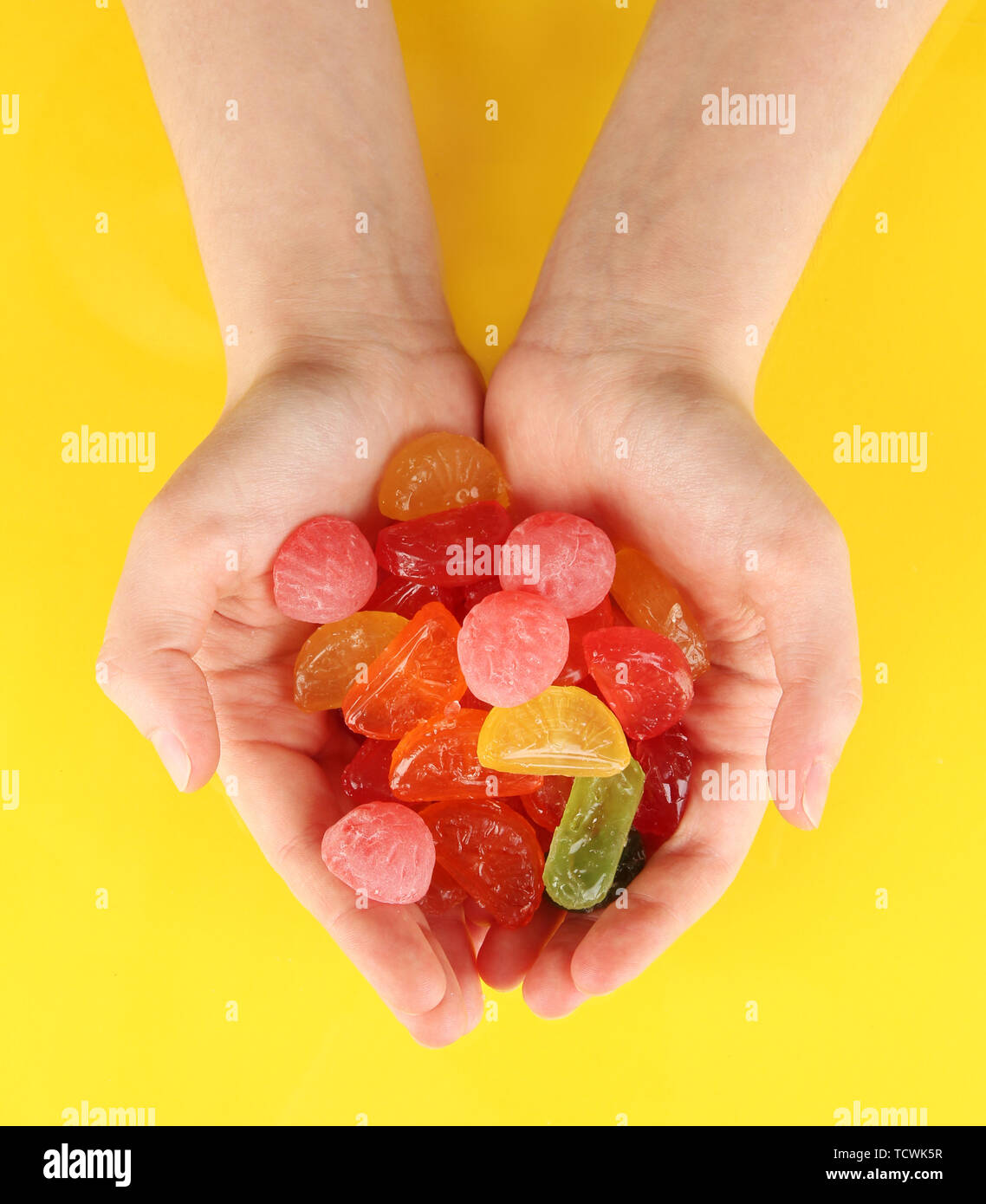 Hands full of sweets on yellow background Stock Photo - Alamy