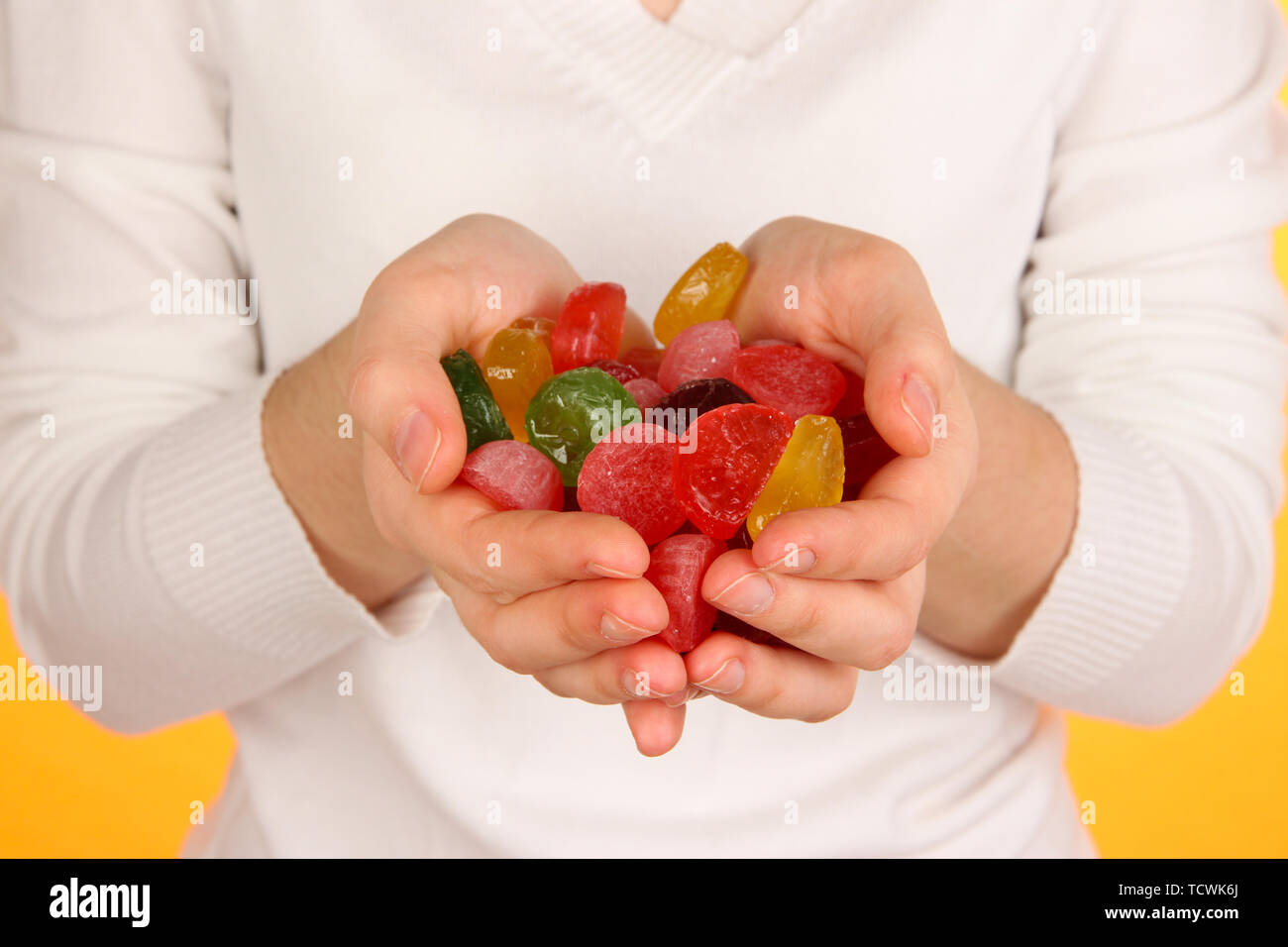 Hands full of sweets on yellow background Stock Photo - Alamy