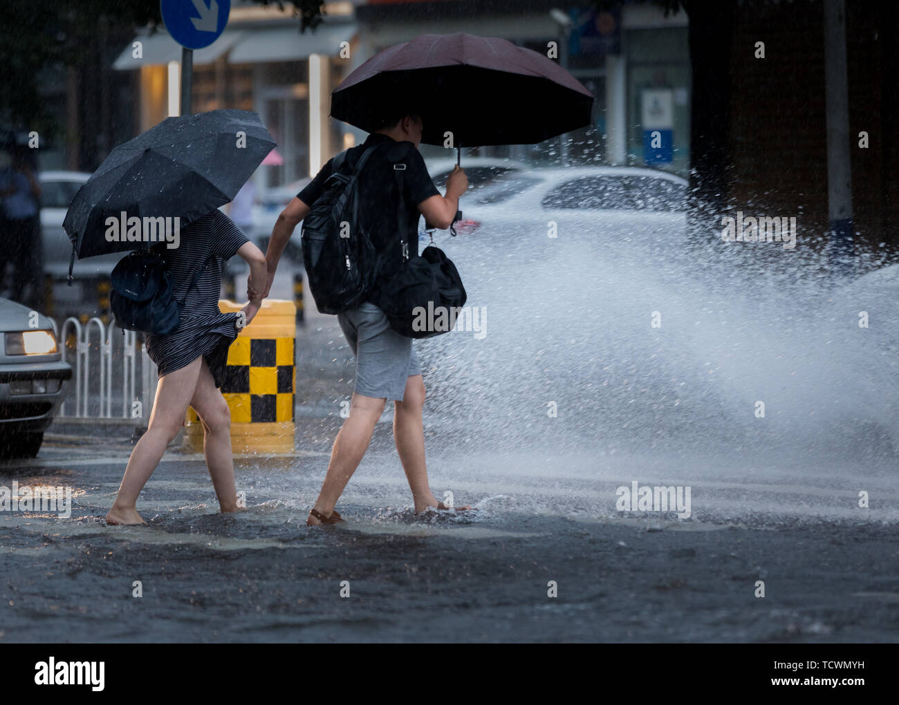 In heavy rain, two people crossing the road encounter a splash of water ...