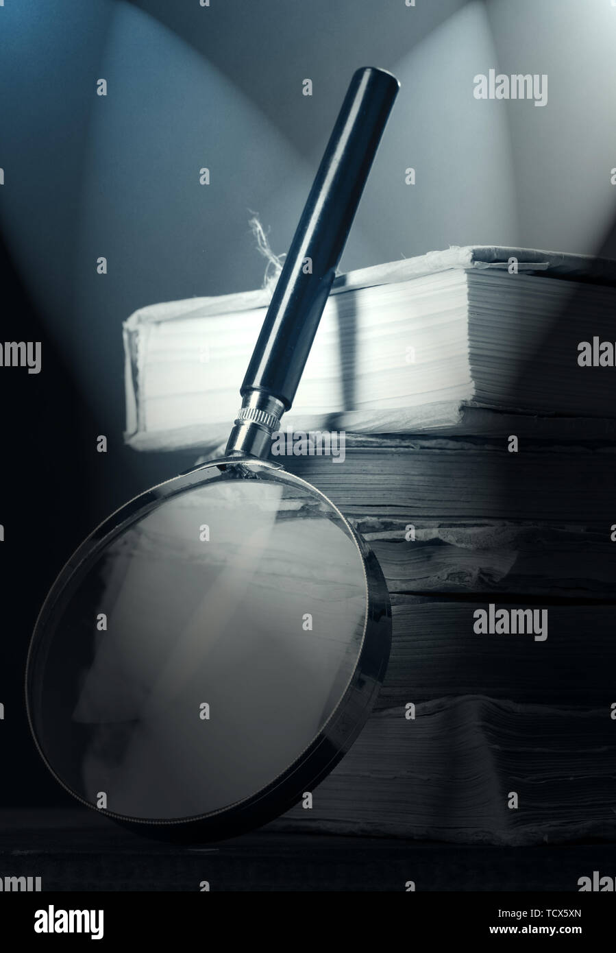 Magnifying glass over the stack of books in dark grey light Stock Photo ...