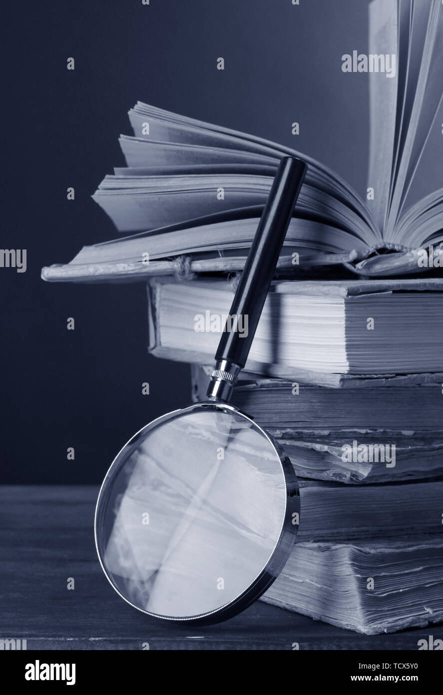 Magnifying glass over the stack of books in grey light on grey ...