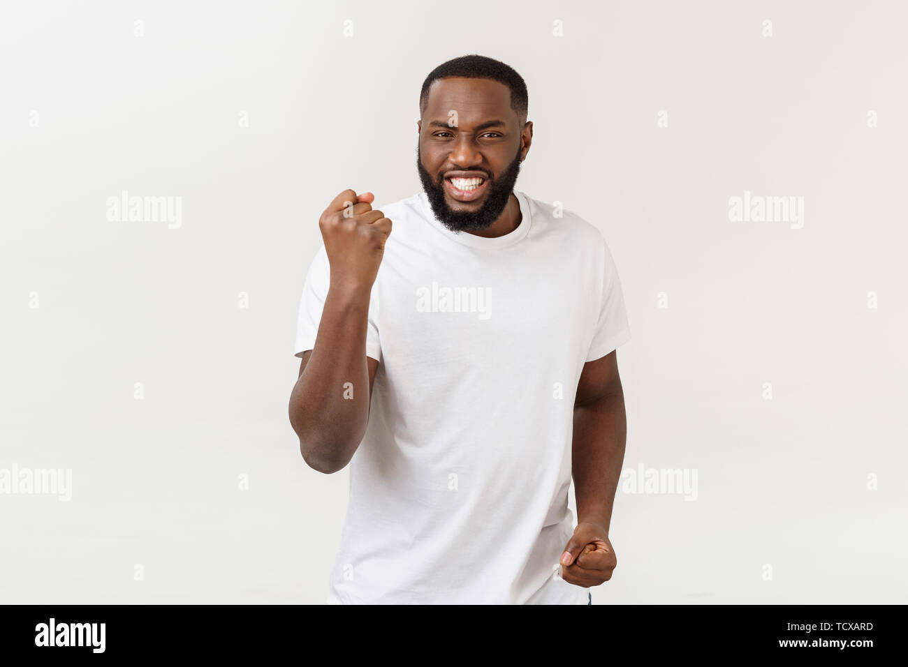 Portrait of a cheerful young man shouting with arms raised in success ...