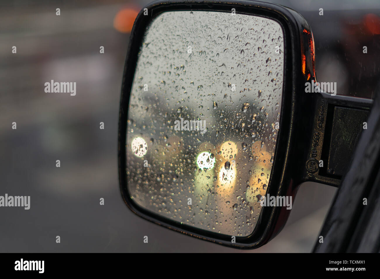 Raindrops on the rearview mirror of a car. In reflection, the ...