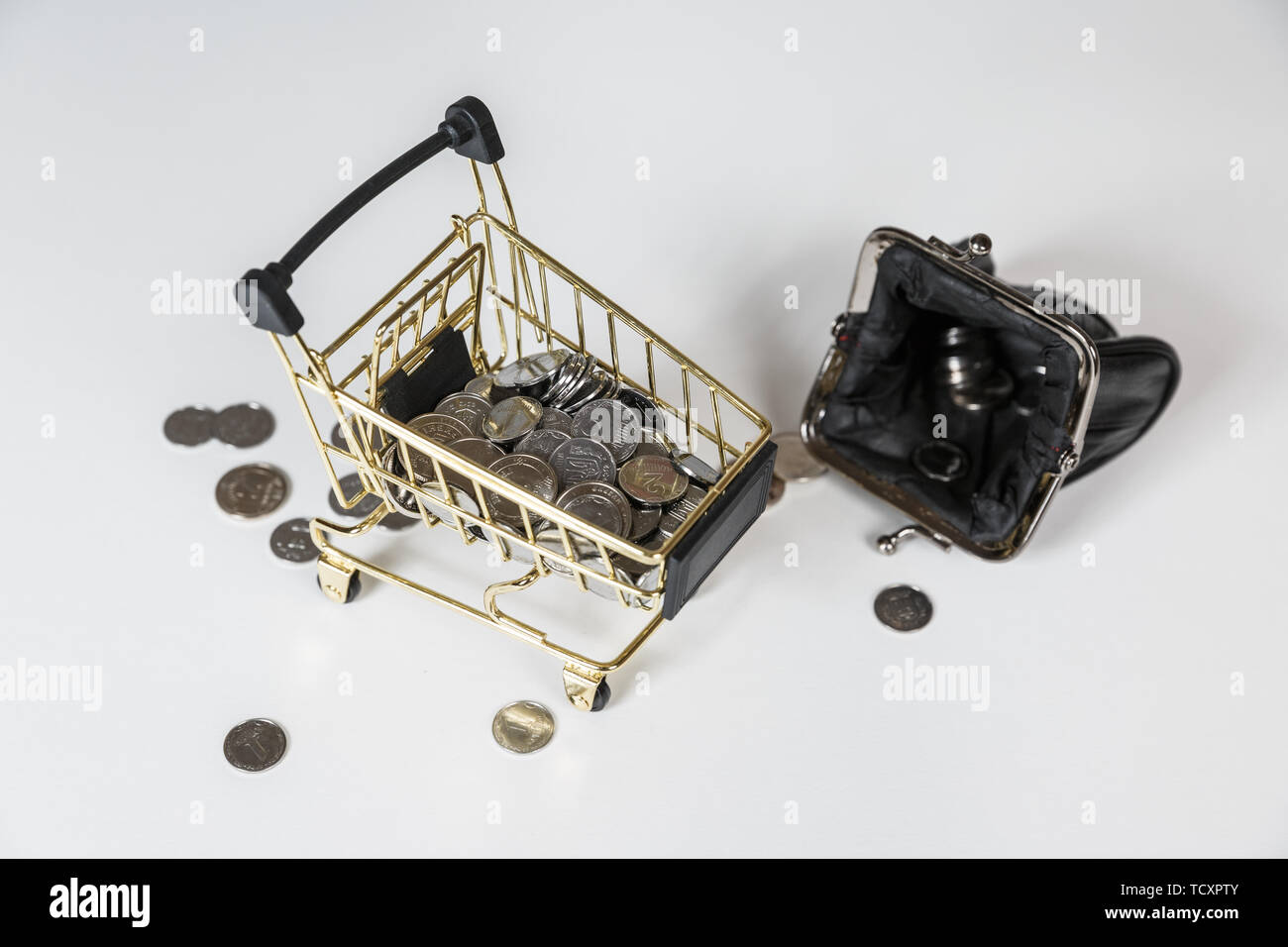 Hand holding a coin with pile of coin in the shopping cart on white and ...
