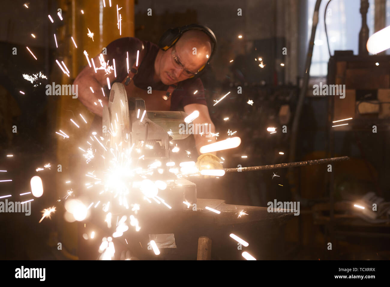 Concentrated young male blacksmith in ear protectors and safety goggles ...