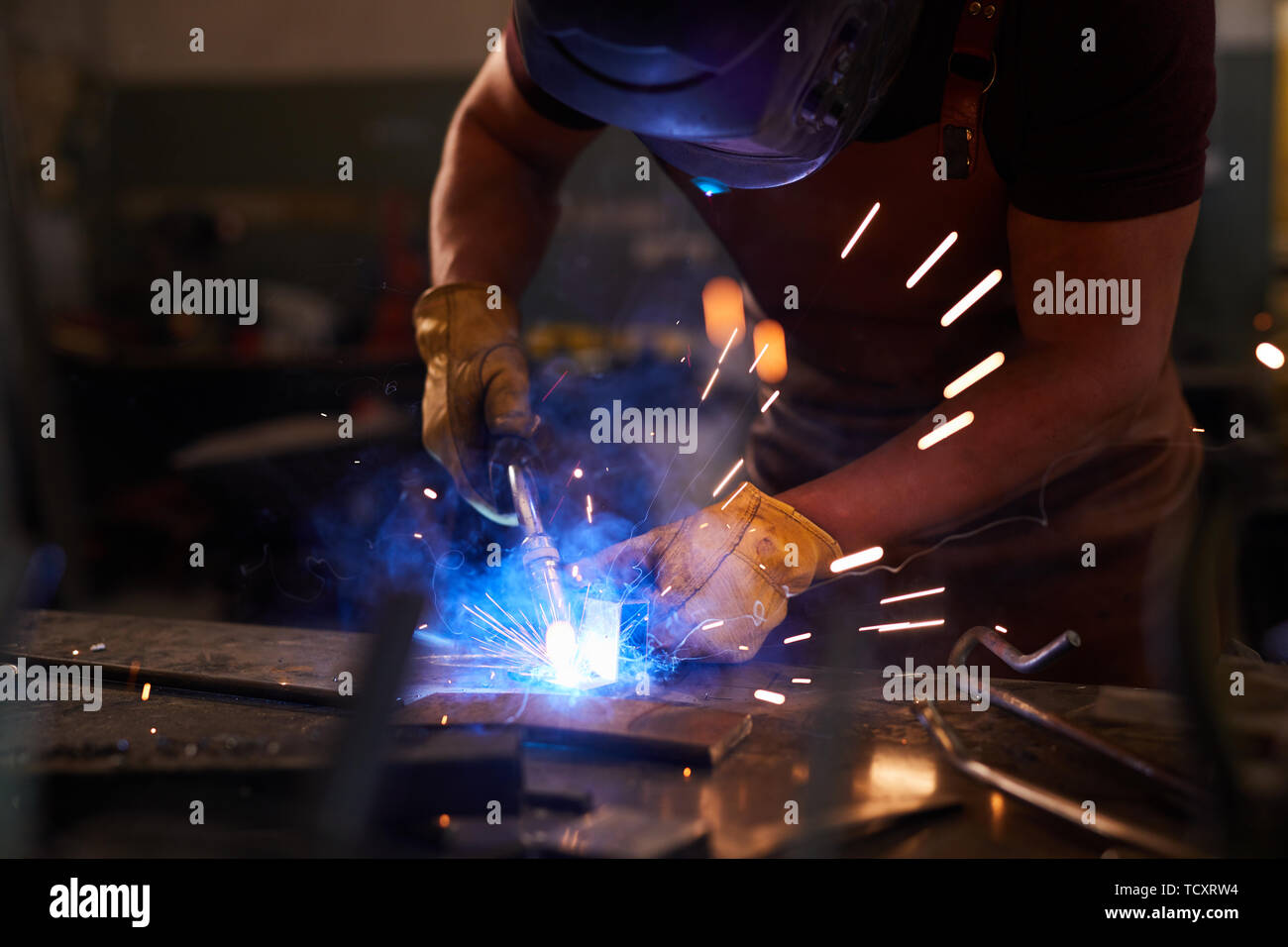 Busy workman in gloves and apron standing at metal table and binding ...