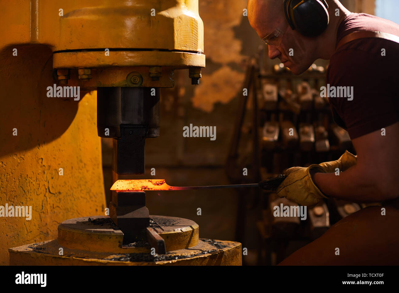 Concentrated bald blacksmith in ear protectors and safety goggles ...