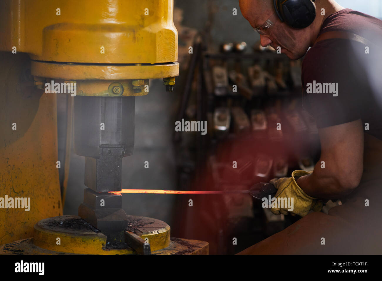 Serious experienced blacksmith in safety goggles holding heated bar ...