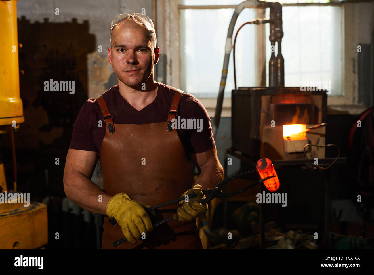 Content young male metalworker in leather apron and safety goggles on ...