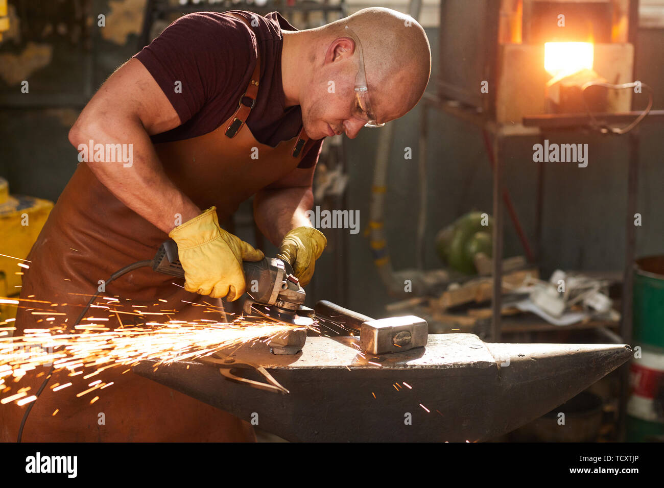 Concentrated busy young workman in safety goggles and leather apron ...