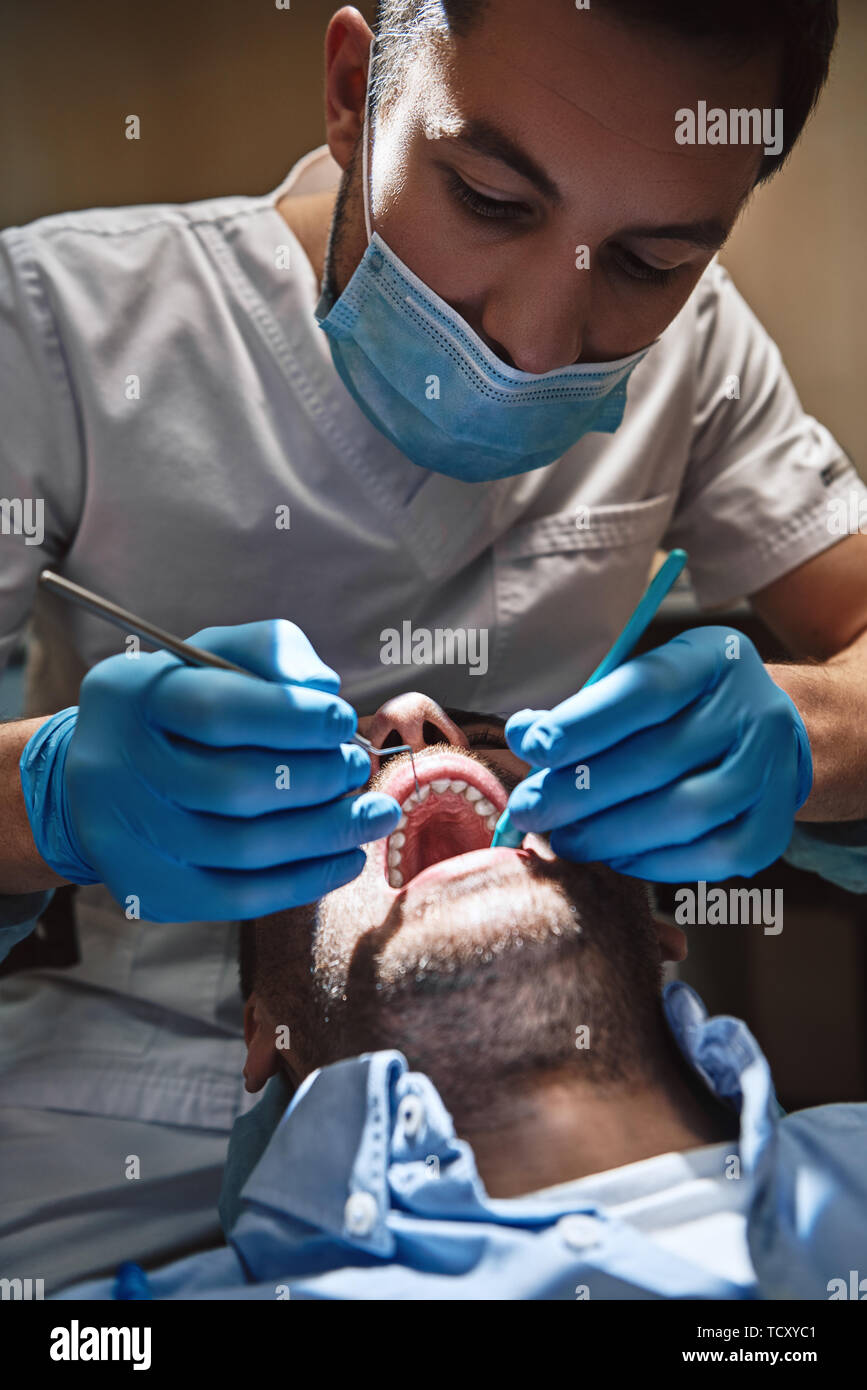 Cropped view of male dentist wearing white uniform, checking up patient ...