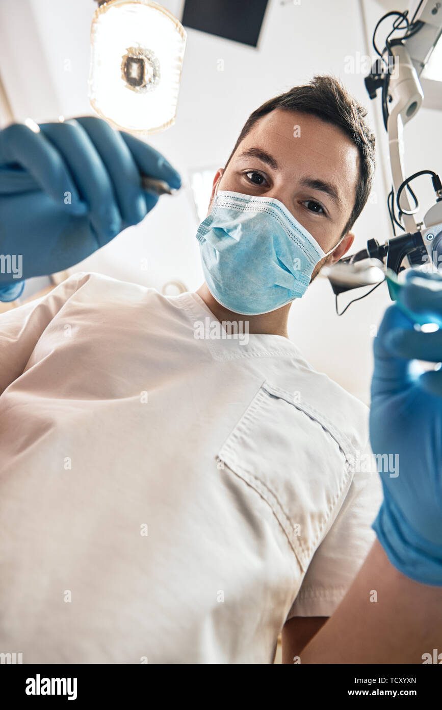 Attractive young dentist is treating his patient. He is standing and ...