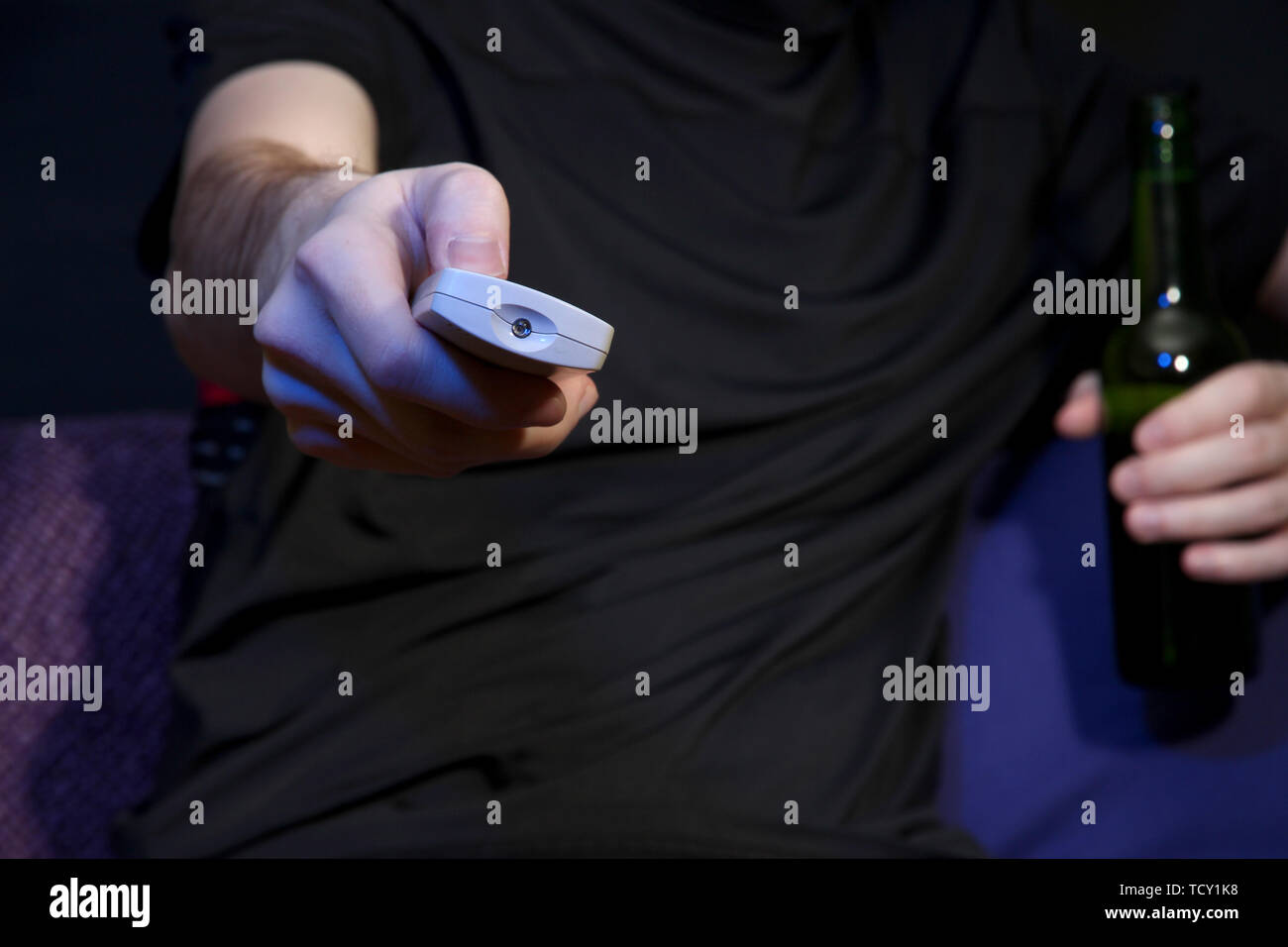 Man hand holding a TV remote control and beer bottle, on dark ...