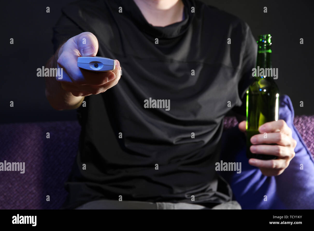 Man hand holding a TV remote control and beer bottle, on dark ...