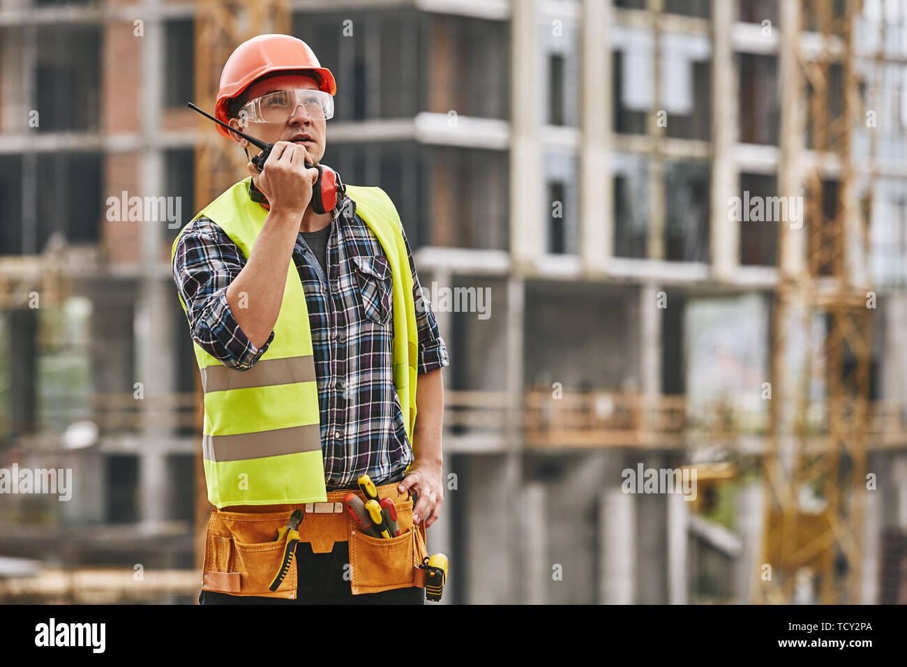 ?hecking work. Professional young builder in working uniform and red ...