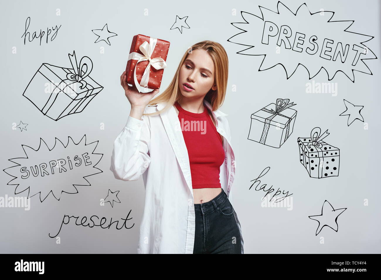 What is inside? Attractive young woman is holding a gift box and trying ...