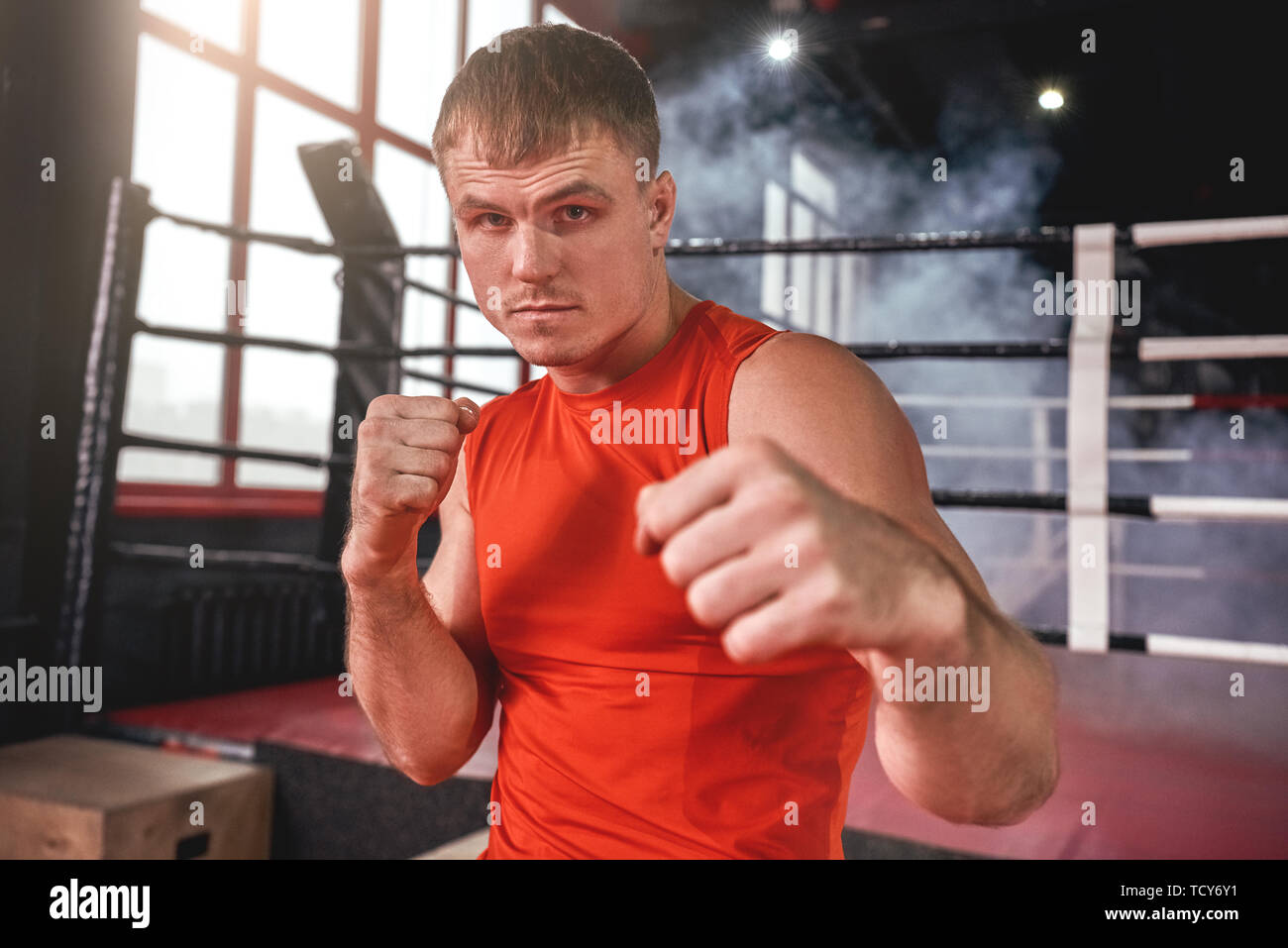 Close-up of focused young muscular boxer athlete in red sports clothing ...