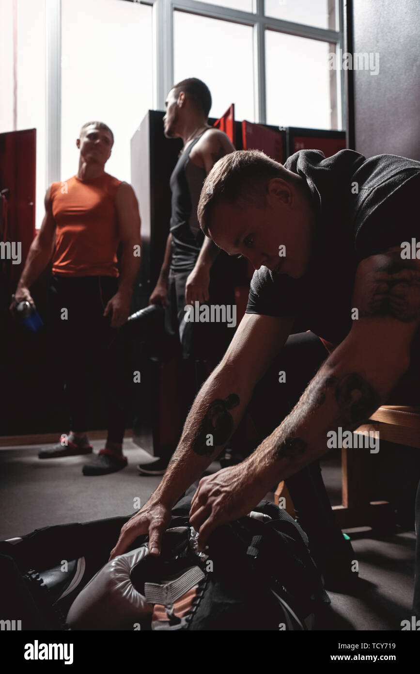 Muscular young athlete boxer in sports clothing getting boxing gloves ...