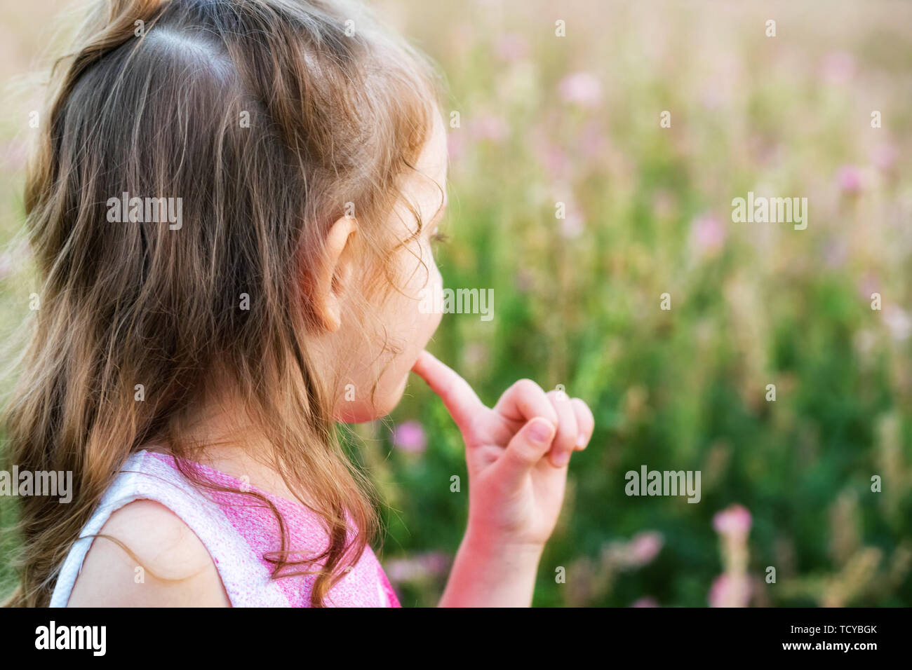 Cute baby girl looks back outdoors in green field. Child portrait Stock ...