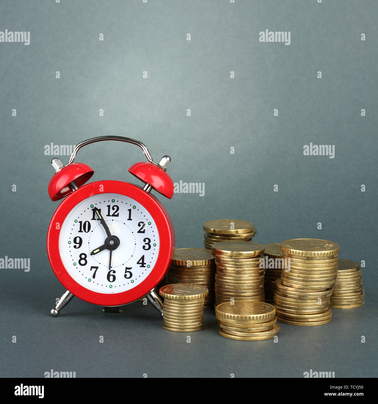 Alarm clock with coins on grey background Stock Photo - Alamy