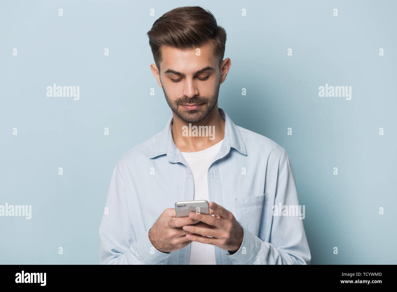 Serious guy holding smartphone standing isolated on blue studio ...