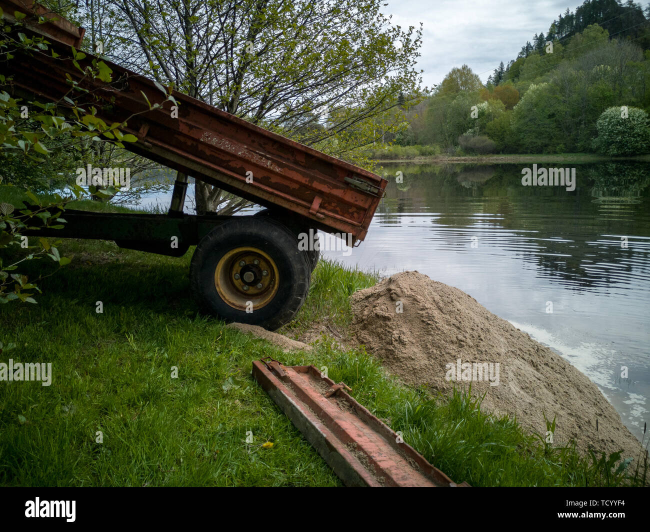 Old tractor trailer tipping a load of sand on the river bank to make a ...