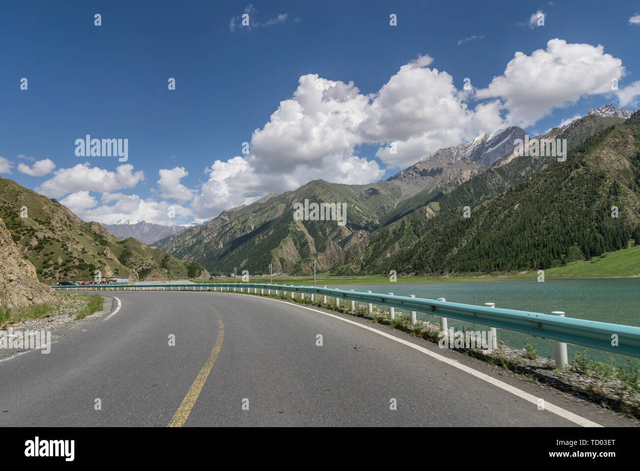 G217 Duku Highway bend in alpine forest under summer blue sky and white ...