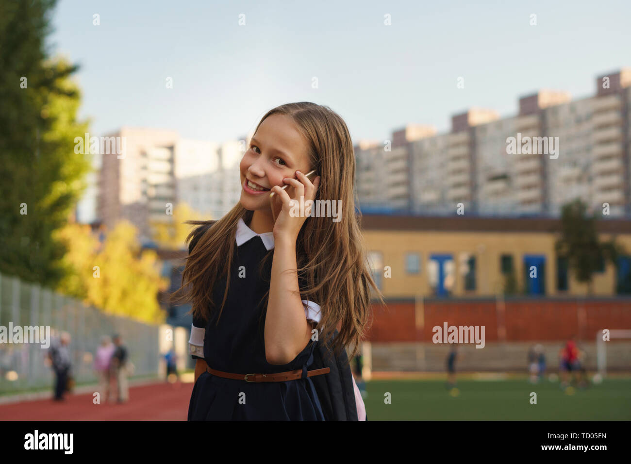 Cute european schoolgirl smiling at the camera, talking on smartphone ...
