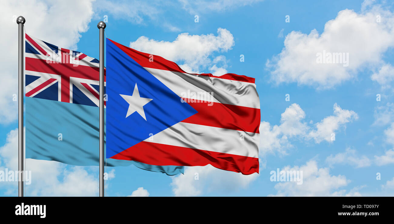 Fiji and Puerto Rico flag waving in the wind against white cloudy blue ...