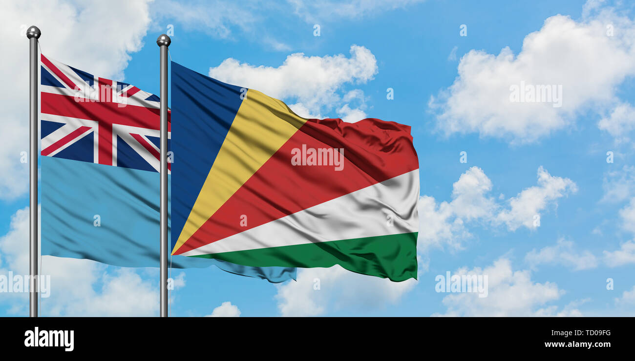 Fiji and Seychelles flag waving in the wind against white cloudy blue sky together. Diplomacy ...