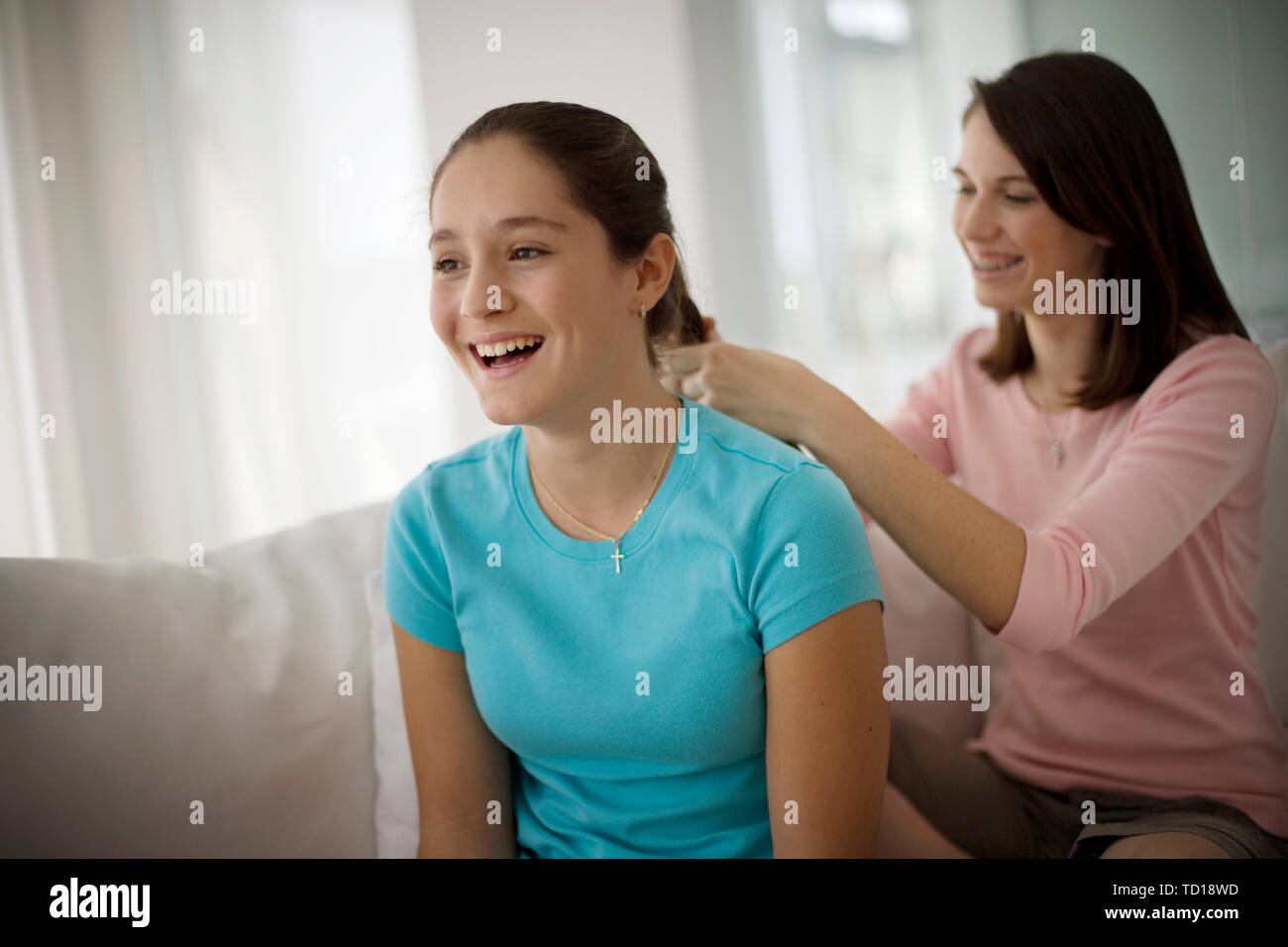 Smiling teenage girl having her hair fixed by her friend sitting on a ...