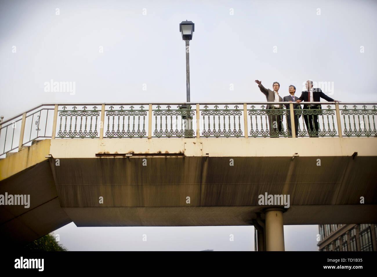 Three businessmen standing on a bridge talking Stock Photo - Alamy