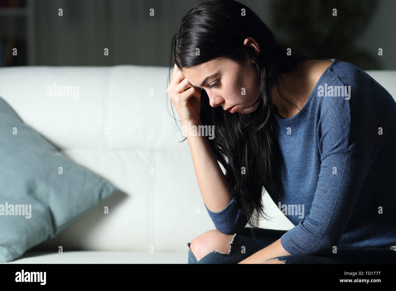 Worried woman thinking alone sitting on a couch in the night at home ...