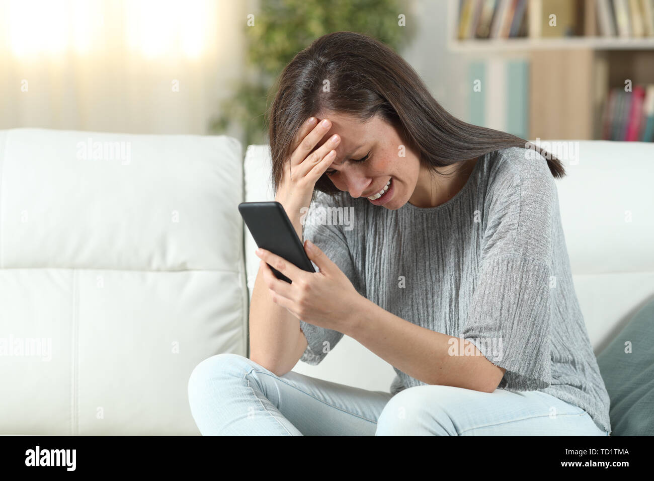 Sad woman checking smart phone sitting on a couch in the living room at ...