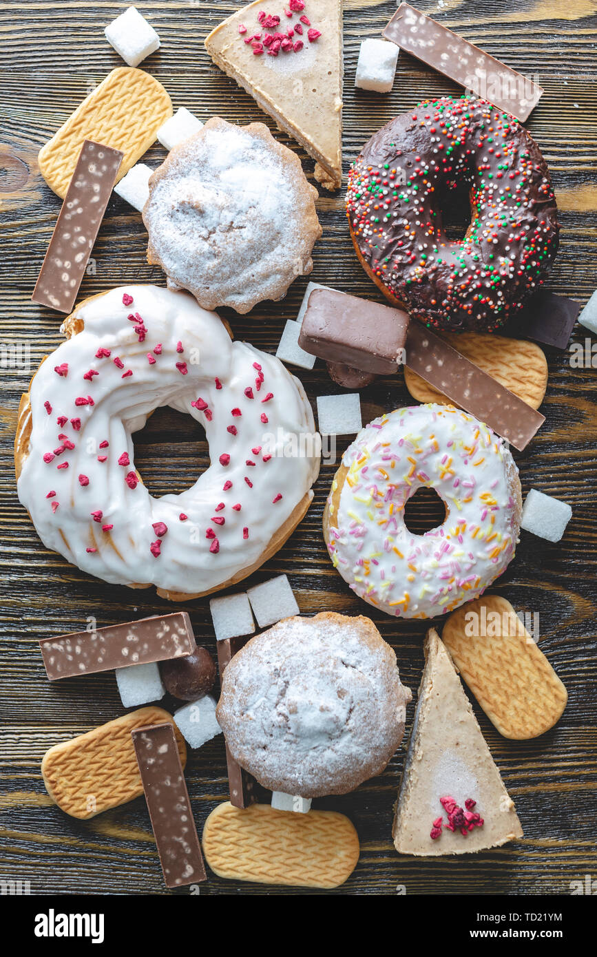 Harmful sweet foods on a dark wooden background. Donuts, muffins ...